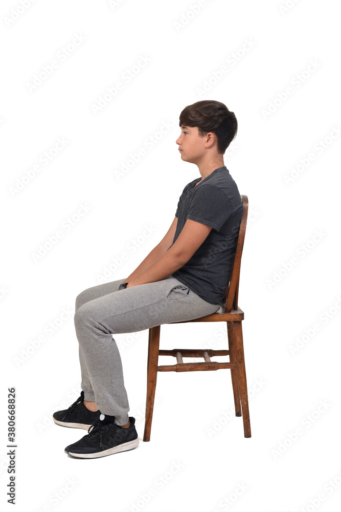 side view of teenage boy sitting on a chair with white background ...