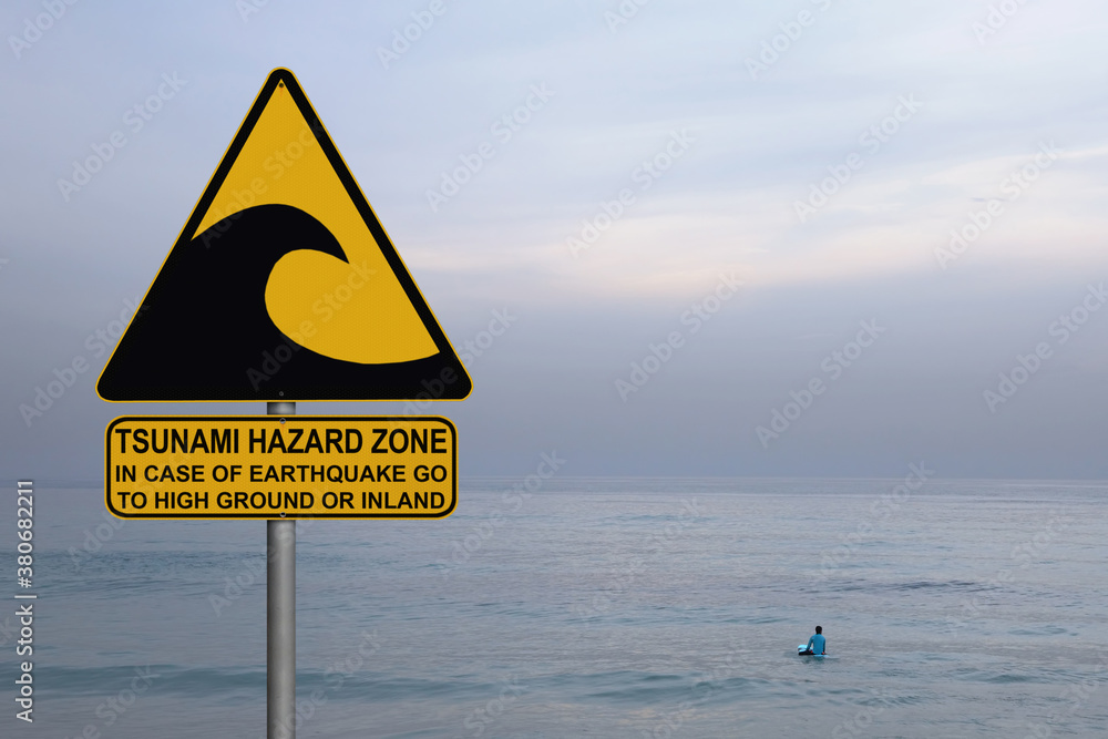 Tsunami warning and evacuation sign located on a beach. Blue calm sea ...
