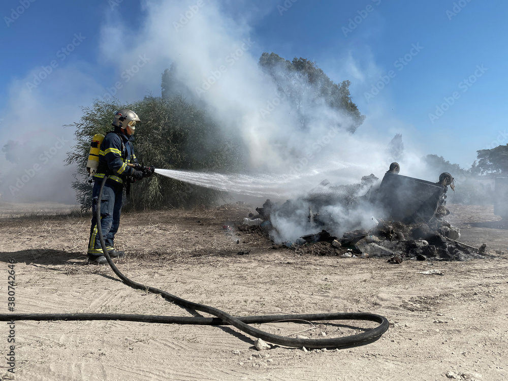 Side view of brave fireman in protective uniform standing with hose and ...