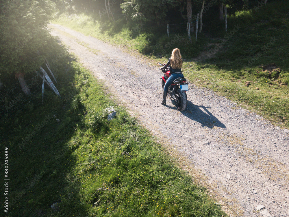 Back view of female biker sitting on parked motorcycle on sandy road in ...