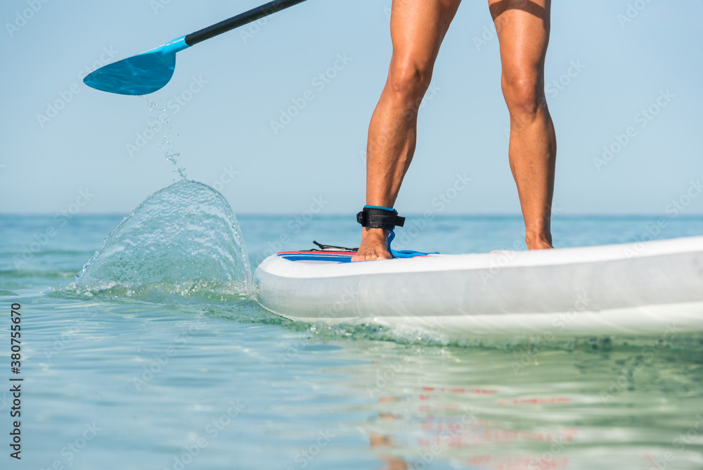 Crop anonymous female surfer standing on surfboard and rowing with ...