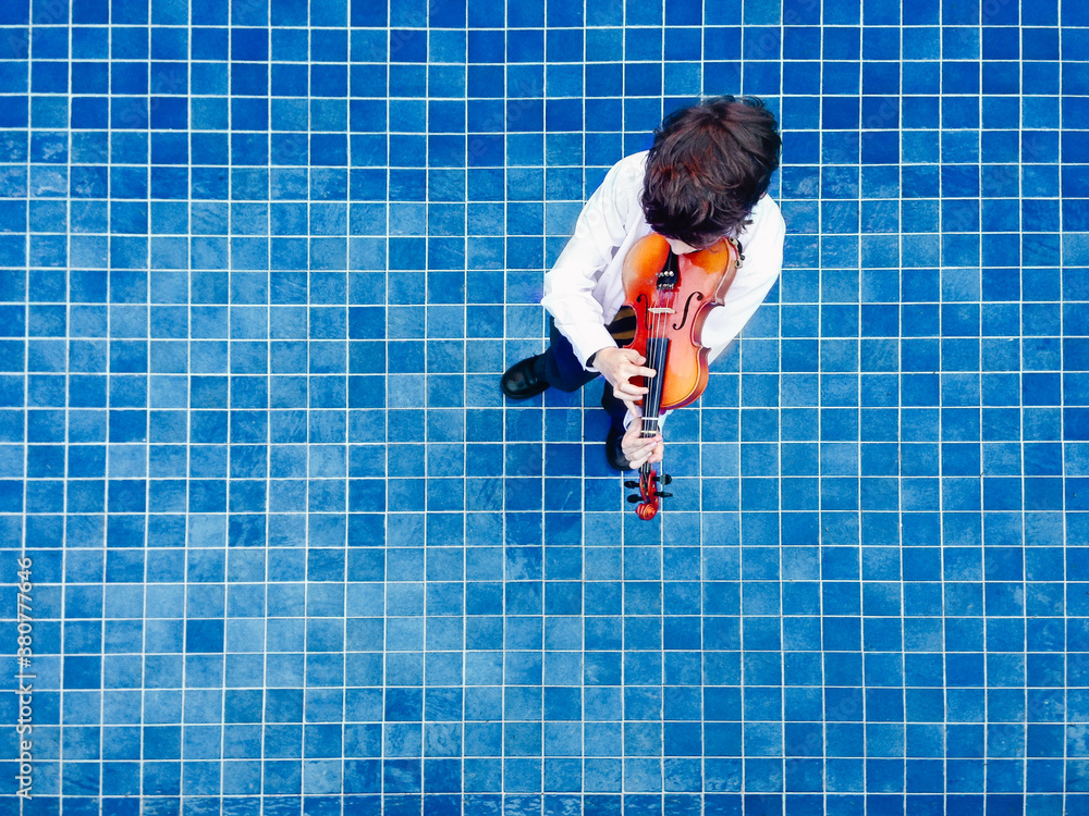 Boy playing a violin in an empty blue tiled swimming pool, viewed from ...