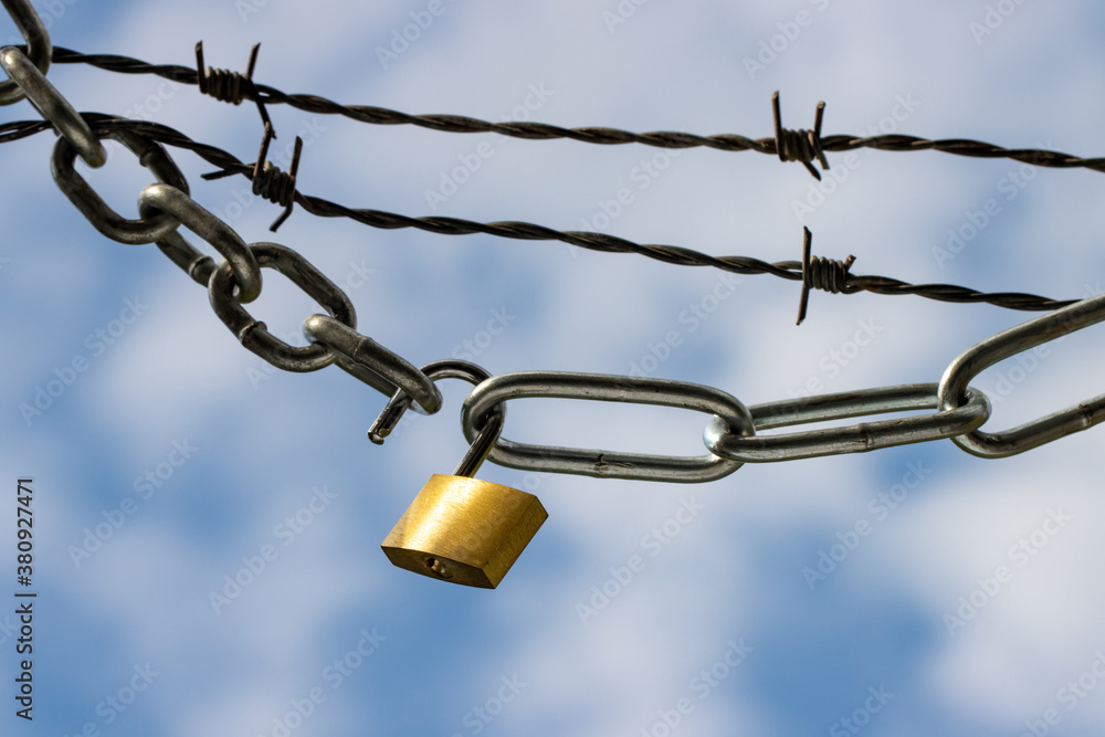 Padlock and steel chains with barbed wire against blue clouded sky ...