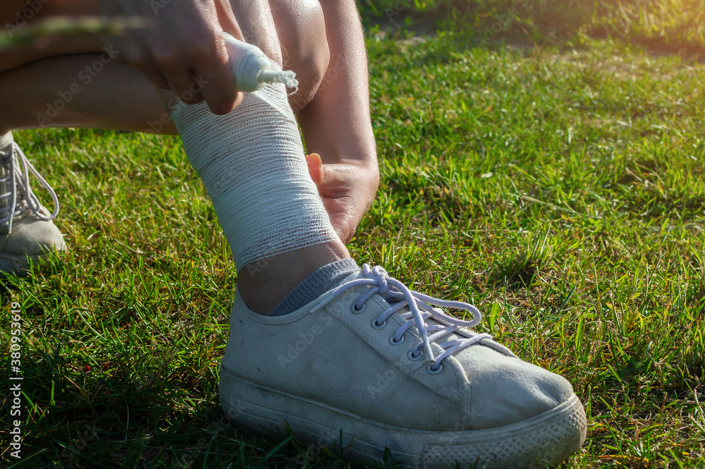 Young woman bandaging injured ankle. Injury leg while running outdoors ...