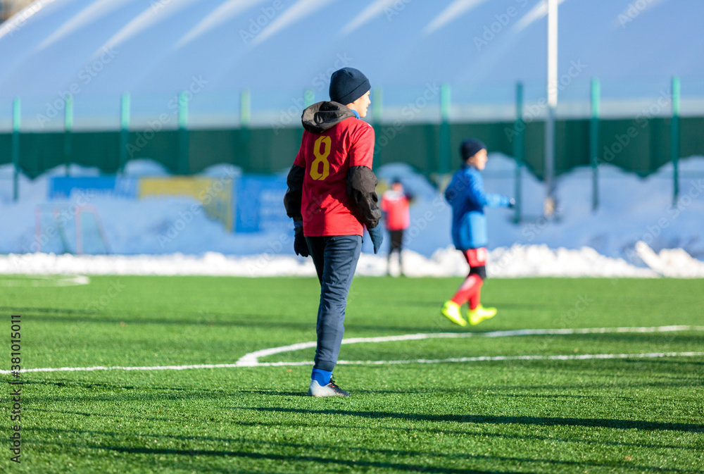 Boys in red sportswear running on soccer field with snow on background ...