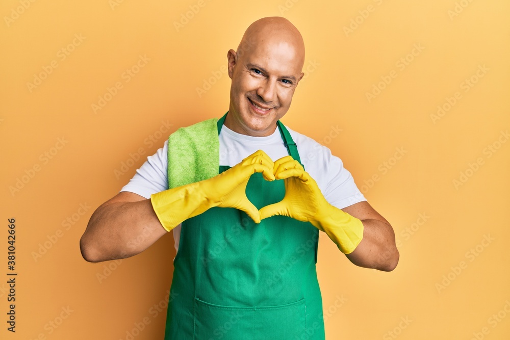 Middle age bald man wearing apron holding cleaning gloves smiling in ...