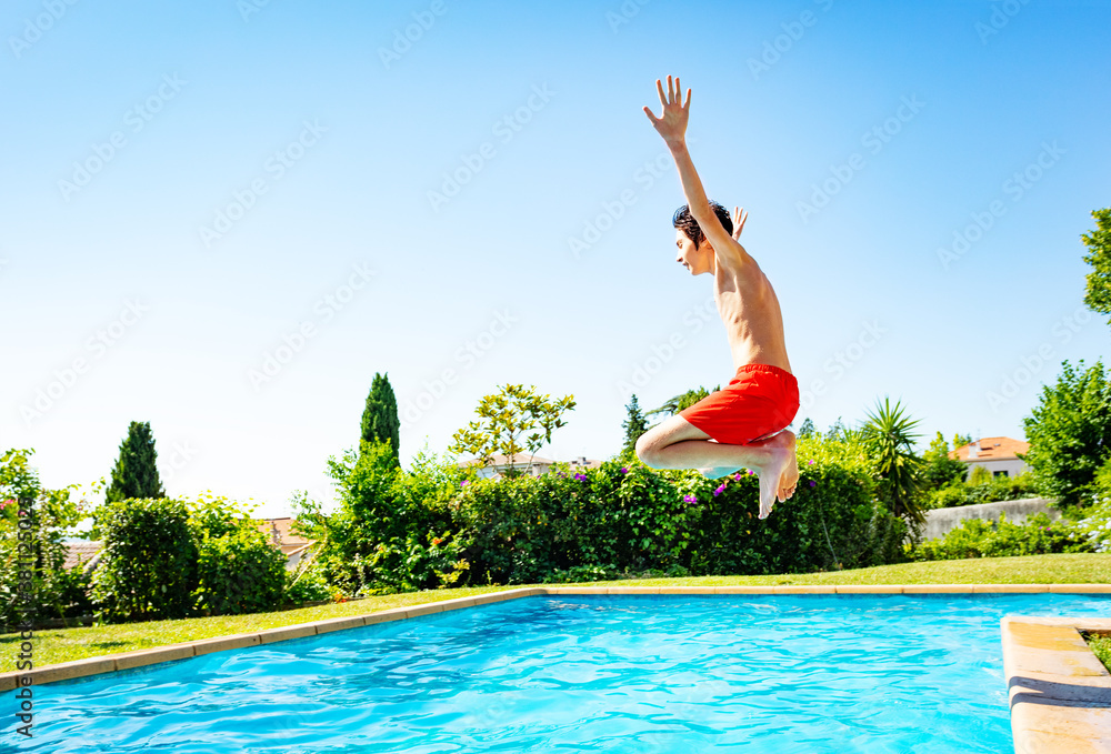Cute boy jump in mid air into the swimming pool water view from side ...