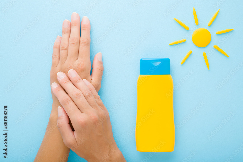 Young woman hands, yellow tube of sunscreen and sun shape on light blue ...