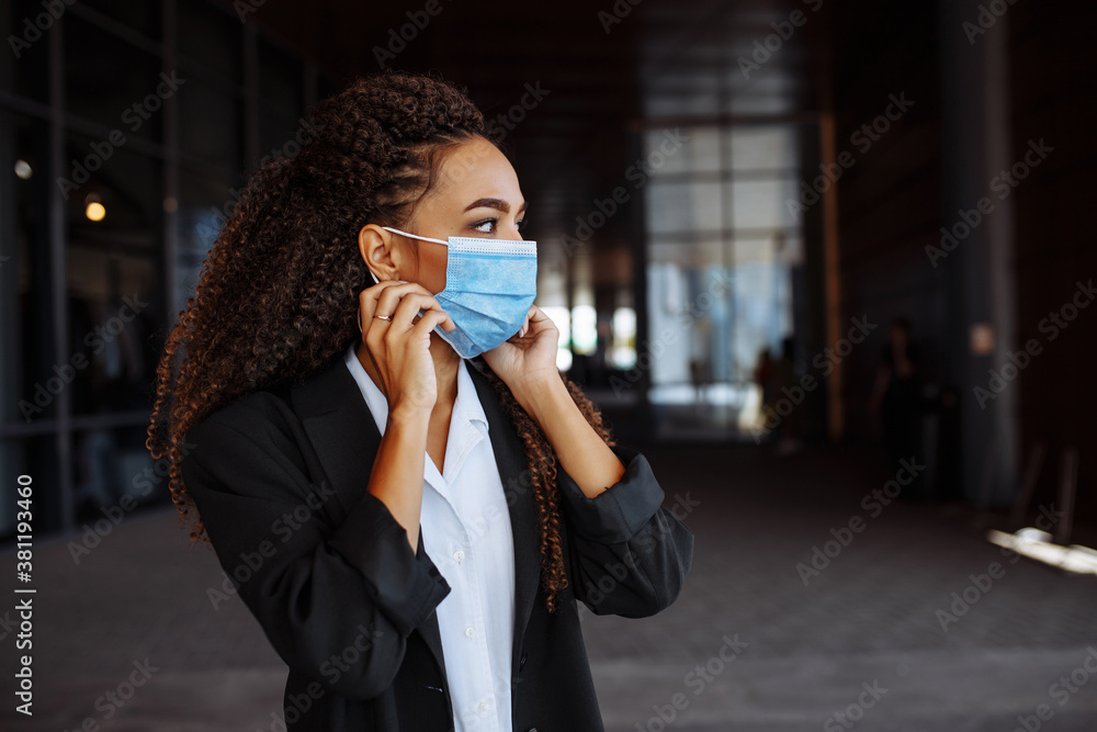 Young officially looking woman in a suit adjusts the medical mask ...