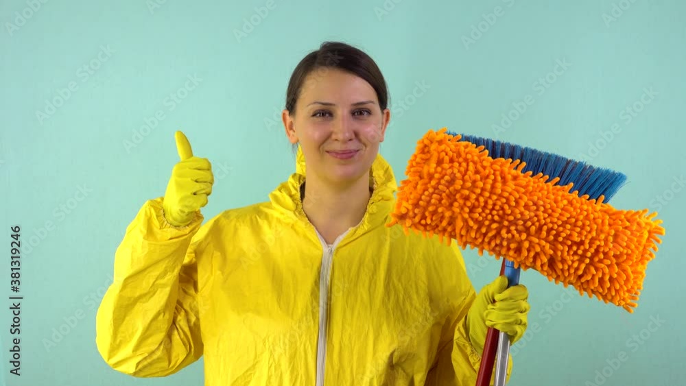 Woman cleaning lady in a yellow suit and gloves with a mop and a broom ...