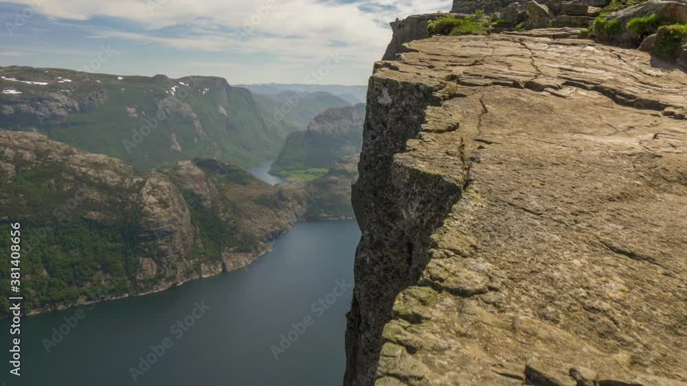 Camera moves along the edge of the cliff. Mountains and fjord seen at ...