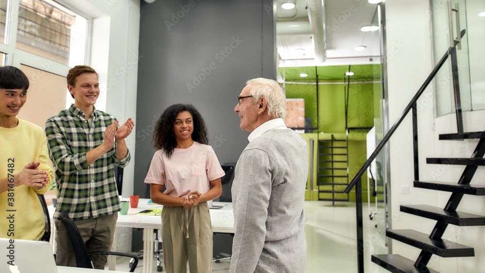 Aged man, senior intern looking pleased while his colleagues praising ...