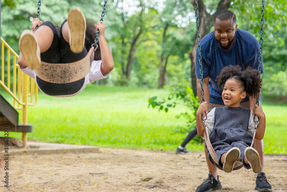 Happy affectionate mixed race family. African man father with two little daughter playing swing ...