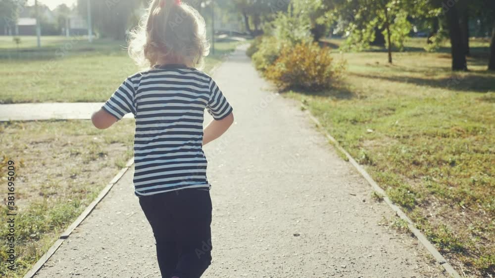 pretty little girl run along the path in the park, view from the back ...