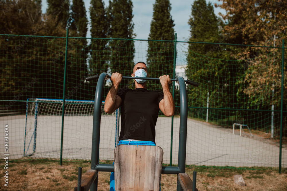Fit young male caucasian athlete with face mask trains on arm and leg ...