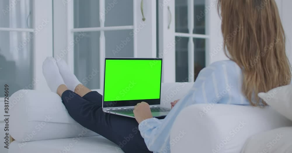 A young woman sits with a laptop on her lap with a green screen during ...