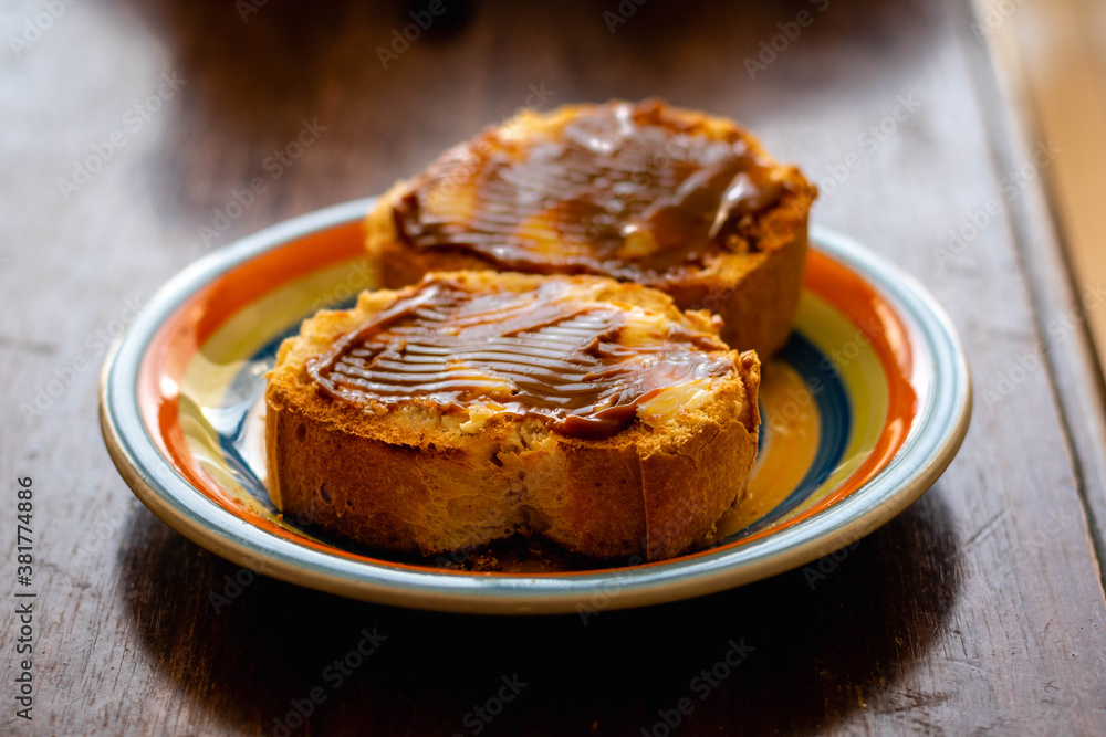 pan tostado con manteca y dulce de leche con luz de mañana sobre plato ...