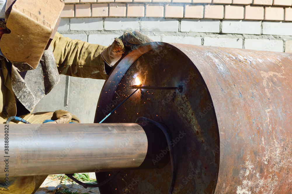 close-up - a worker welds a large iron pipe, holds in his hand a clamp ...