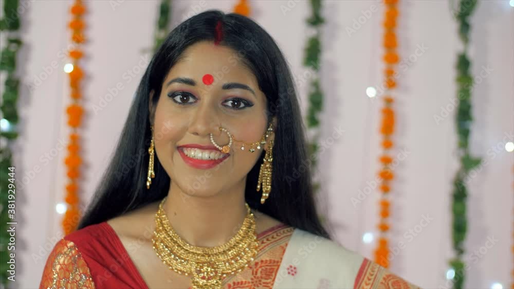 Pretty Bengali woman putting a big red bindi while looking towards the ...