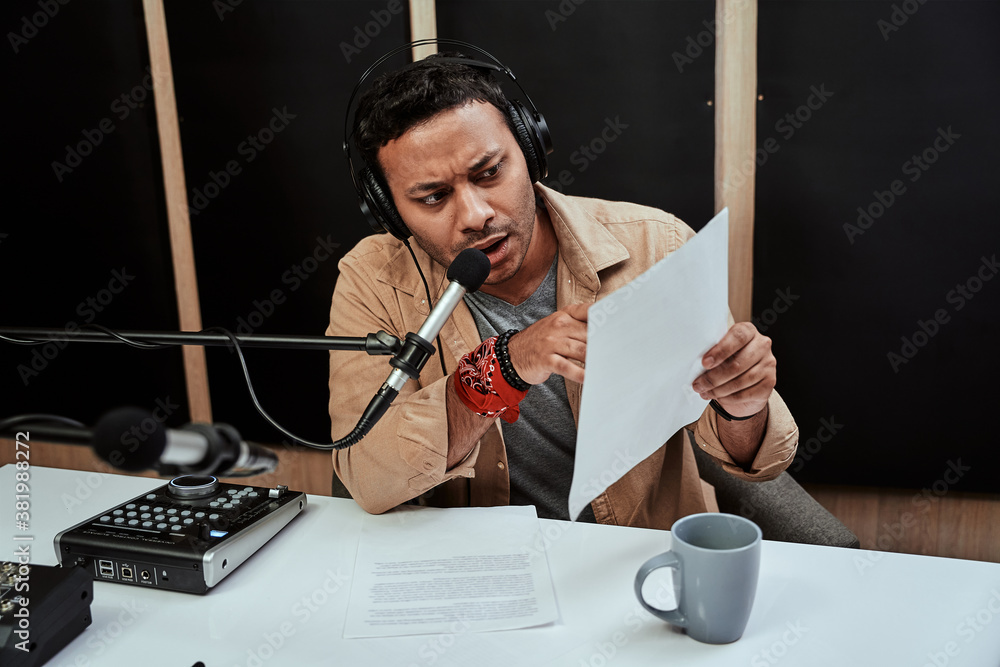 Portrait of young male radio host looking serious while reading a ...