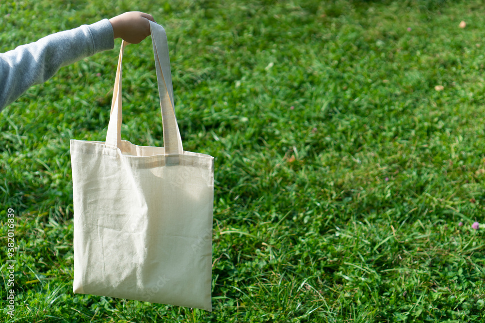 Child hand holding reusable eco bag on green grass background. Ecology ...