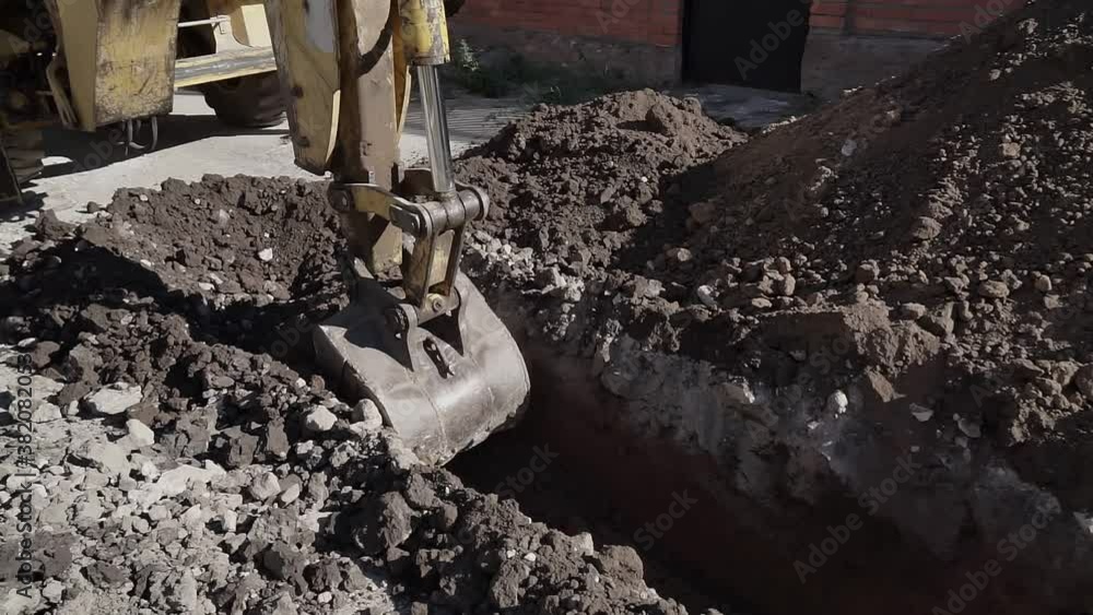 Big metal excavator bucket scoops up dirt while digging a ditch during ...