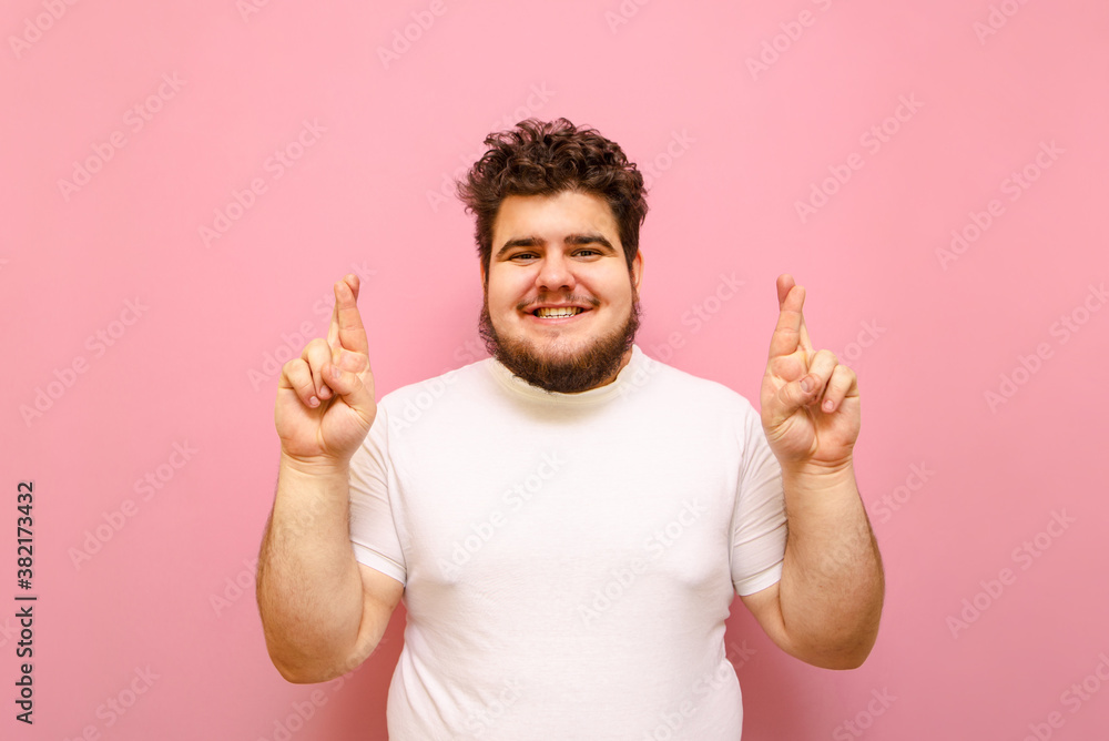 Positive young overweight man standing on a pink background looking ...