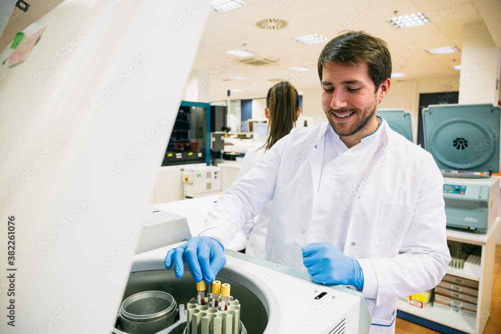 Handsome man in lab coat smiling and using blood analyzer while working ...