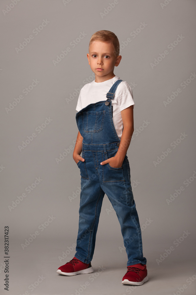 Handsome child guy blond schoolboy in denim overalls in the studio ...