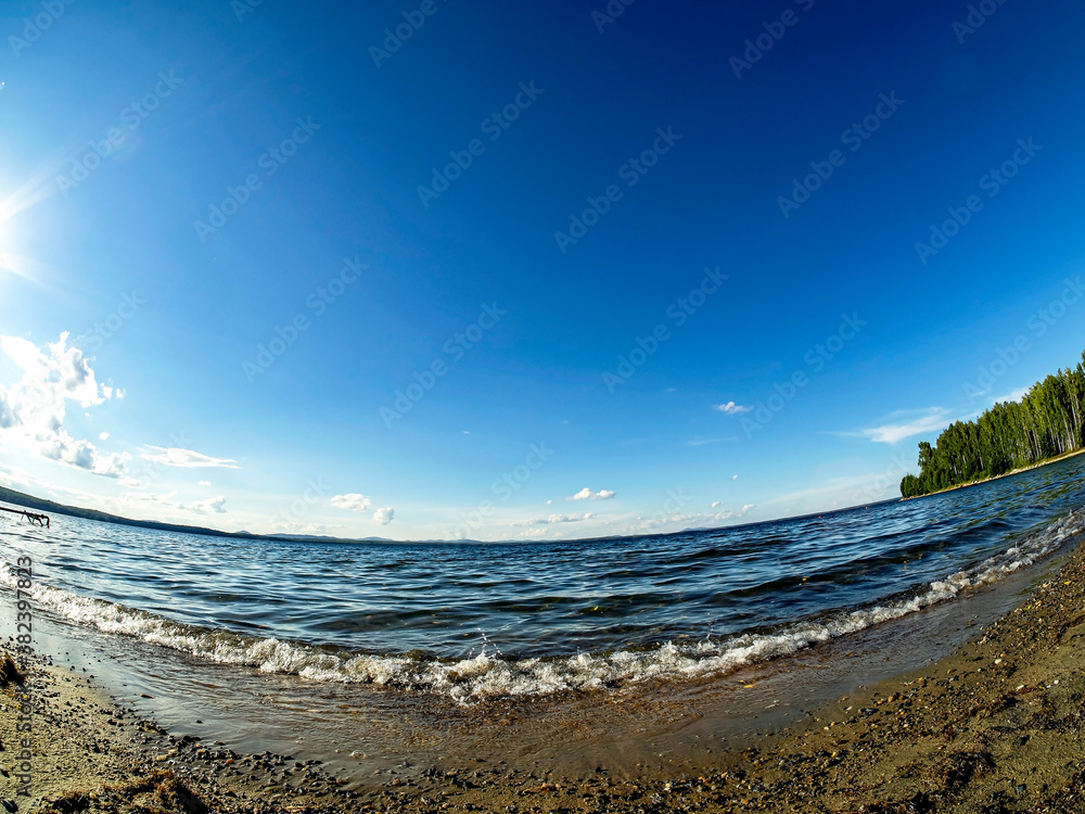shore of the lake, sand, lapping waves, blue sky with light clouds ...