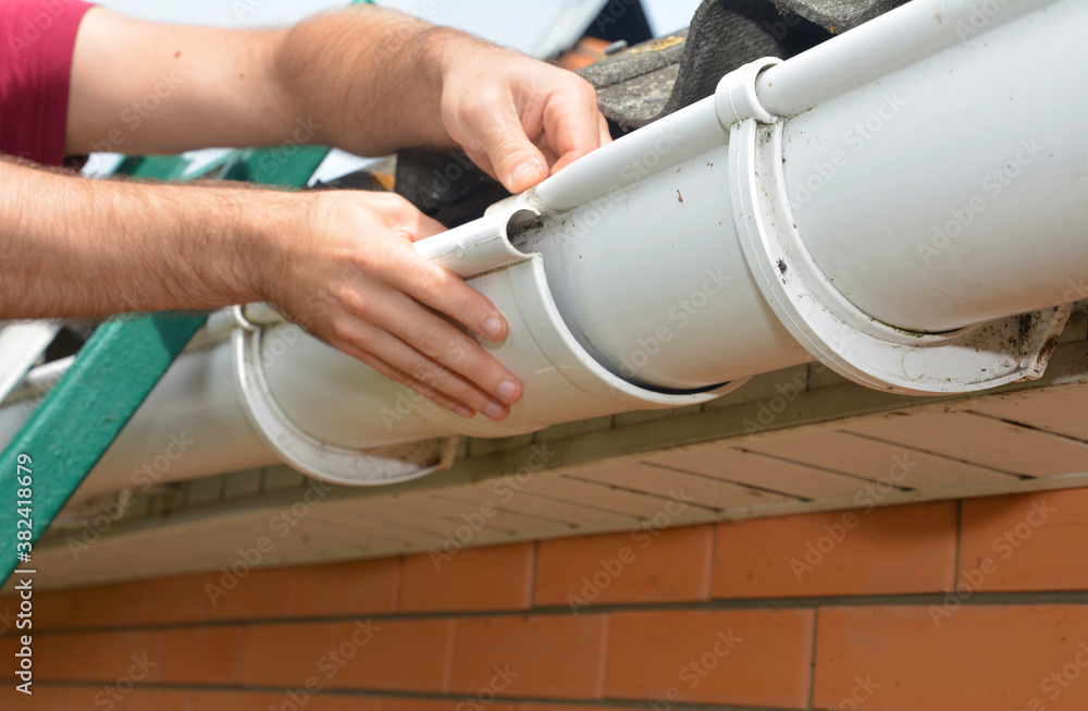 A man is installing, repairing a rain gutter system attaching the union ...