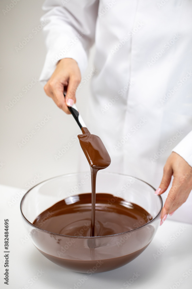 hand of Female Confectioner mixes melted milk chocolate in glass bowl ...