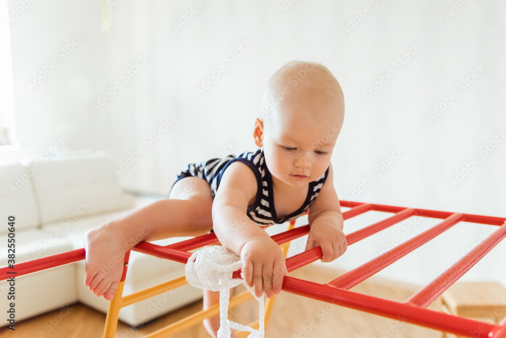 Cute baby performs gymnastic exercises on a wooden home sports complex ...
