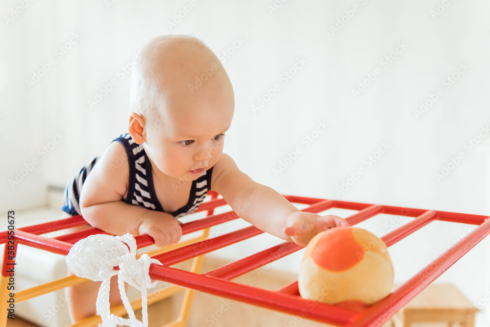 Cute baby performs gymnastic exercises on a wooden home sports complex ...