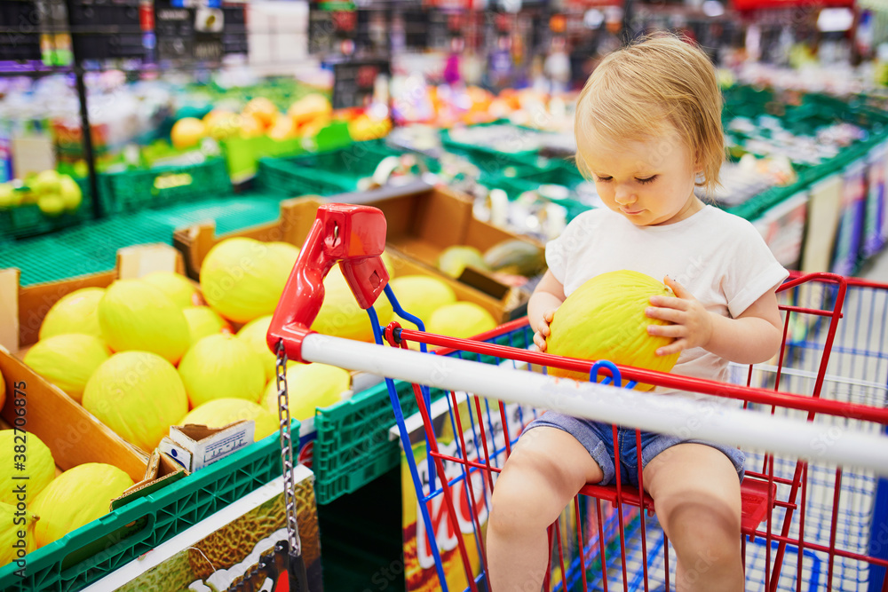 Toddler girl sitting in the shopping cart in a food store or a ...