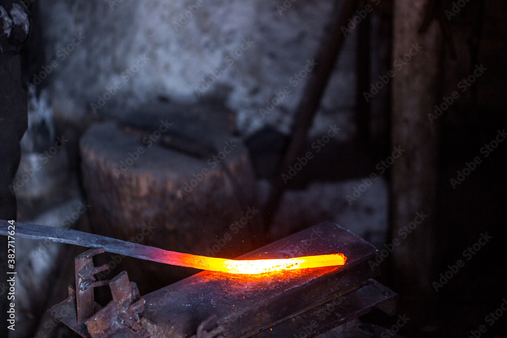 In a blacksmith's workshop. Blacksmith in one hand hold a workpiece of ...