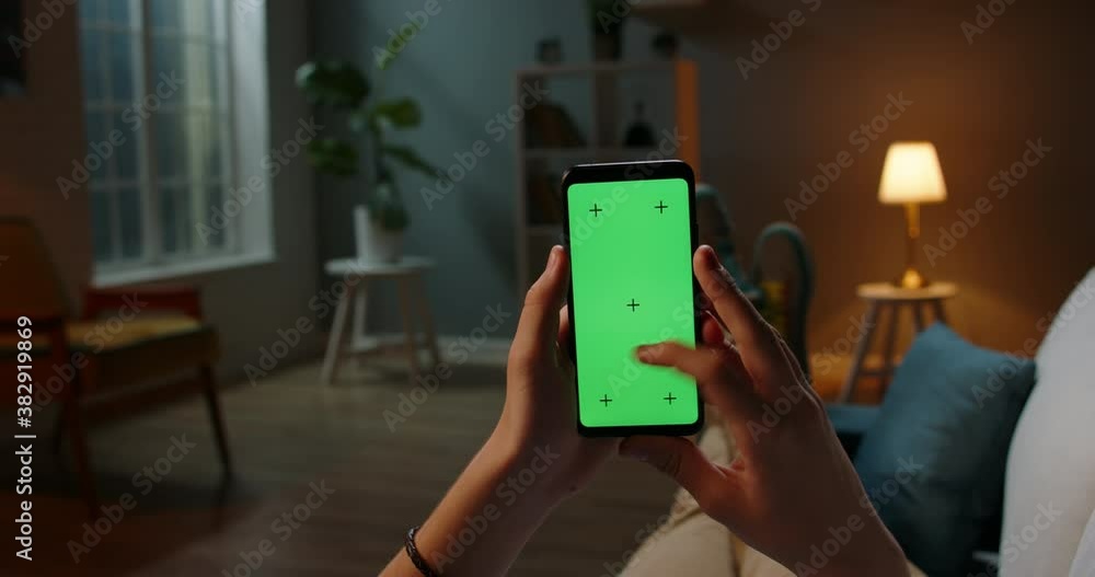 Man lying on couch using smartphone with chroma key green screen at night, scrdoing various ...