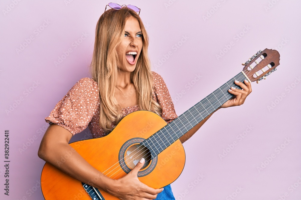 Beautiful blonde young woman playing classical guitar angry and mad ...