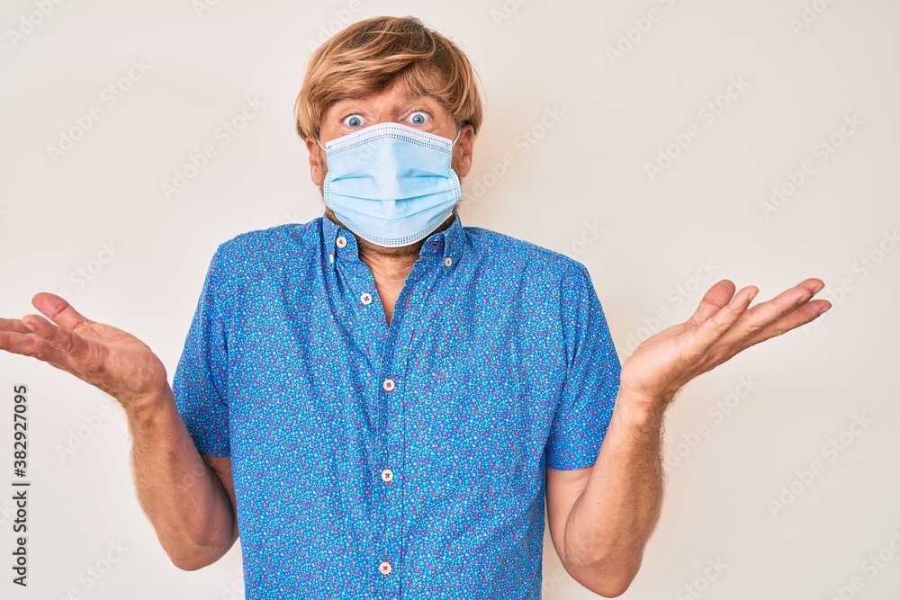 Young blond man wearing medical mask clueless and confused with open ...