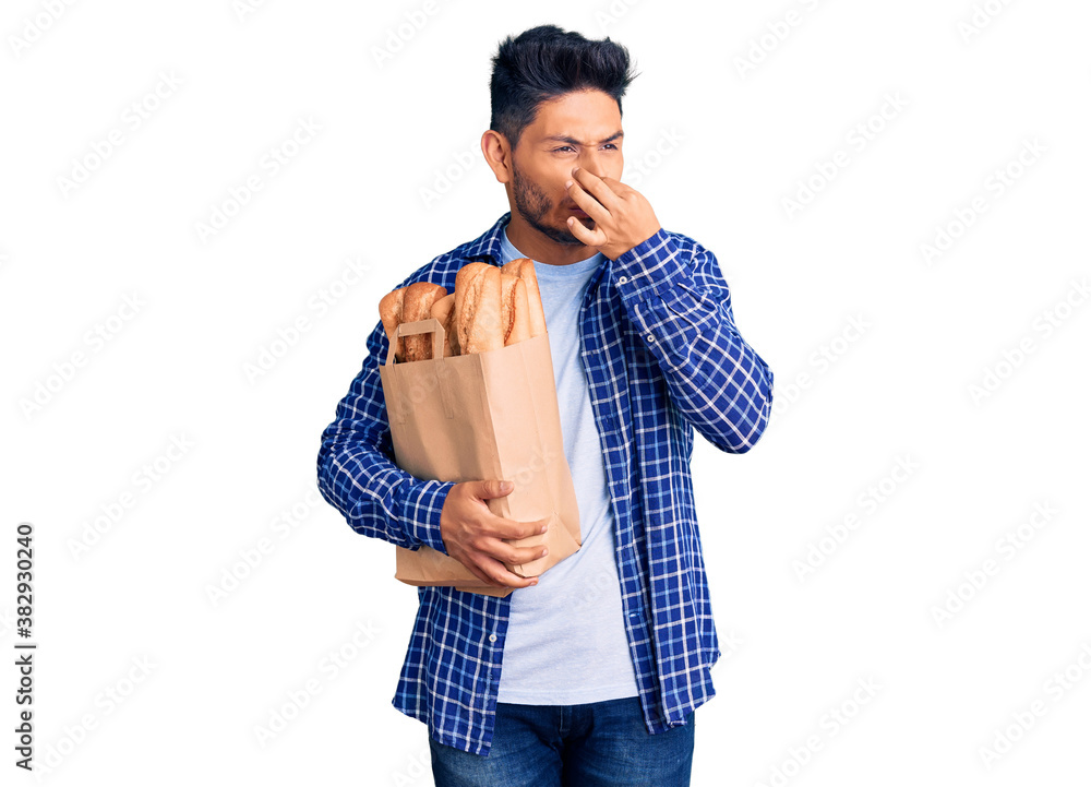 Handsome latin american young man holding paper bag with bread smelling ...