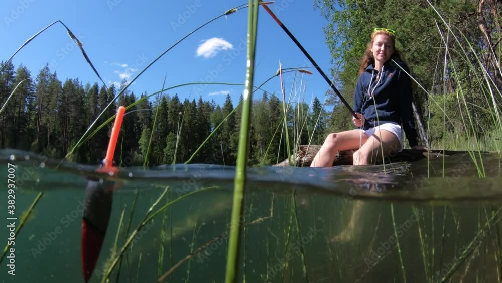 Young woman fishing on a forest lake's coast with underwater view of ...
