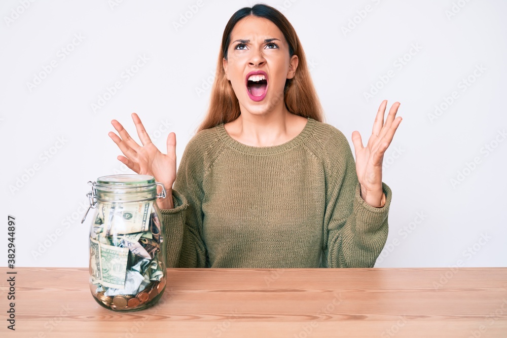 Young brunette woman sitting on the table with jar full of dollars ...
