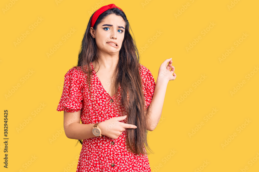 Brunette teenager girl wearing summer dress pointing aside worried and ...