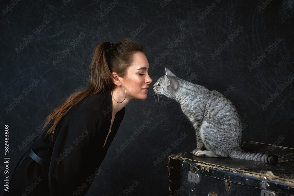 portrait of a young woman with a cat on a dark background . Man and ...