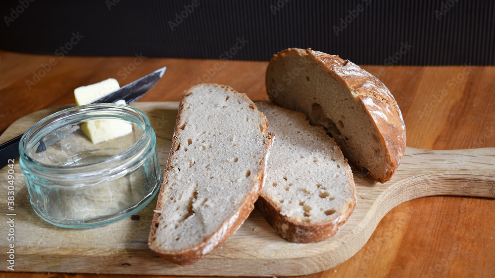 Bauernbrot aufgeschnitten in Brotscheiben mit Brotmesser, Glas, Butter ...