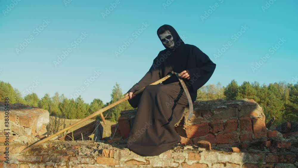 Creepy grim reaper, angel of death, in black cloak sitting on ruined ...
