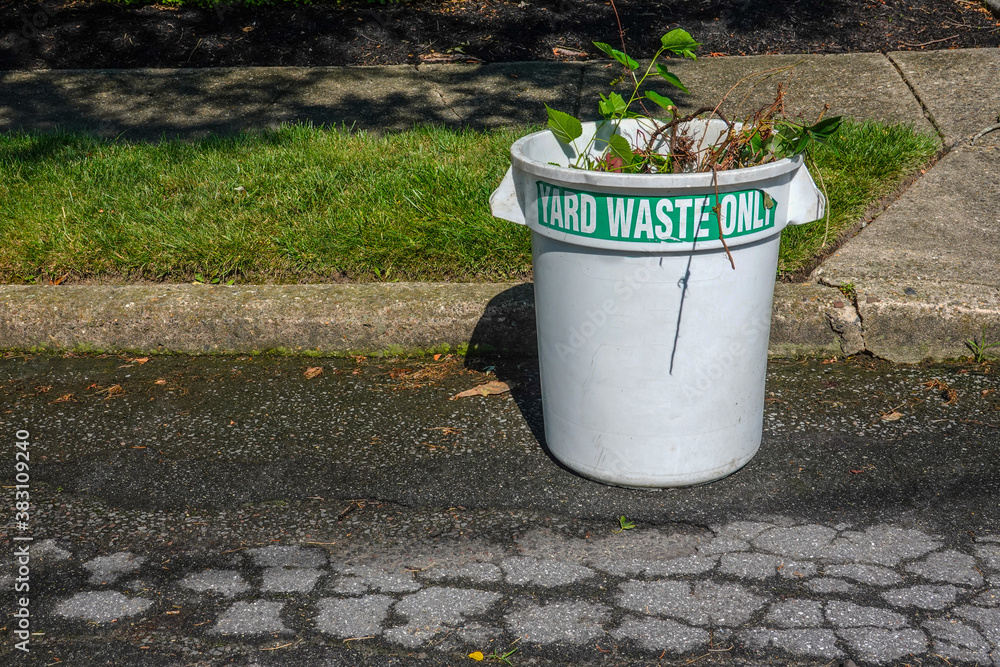 White trash can labeled yard waste full of plant debris on an asphalt ...