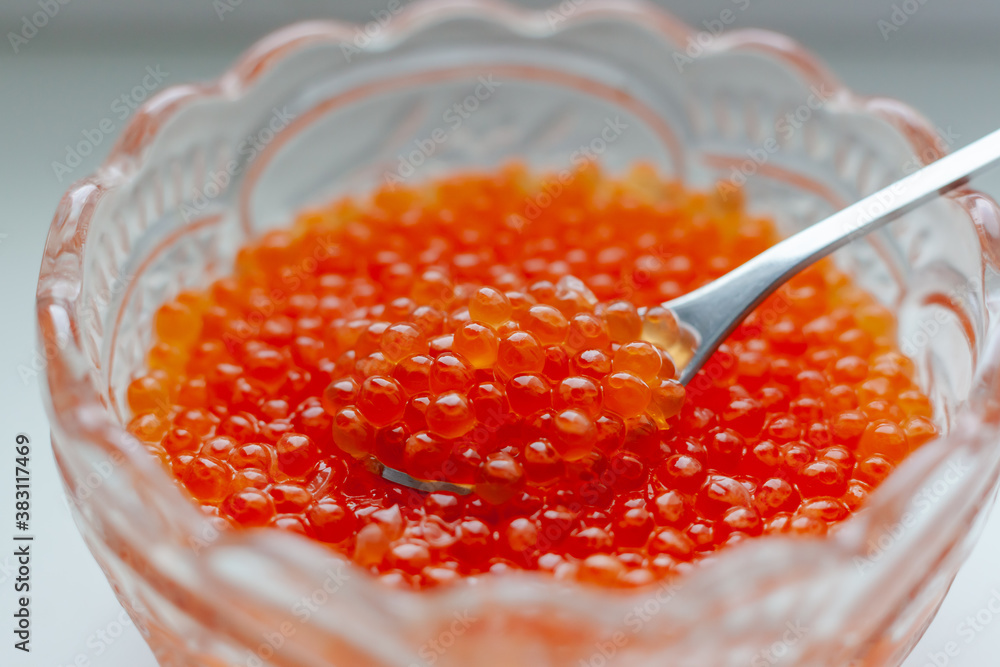 Red caviar in a transparent crystal plate, in a plate is a metal spoon ...