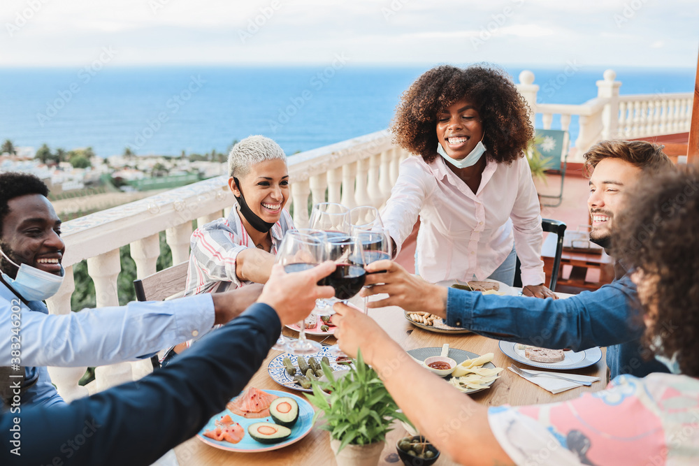 Young multiracial people cheering with wine while wearing protective ...