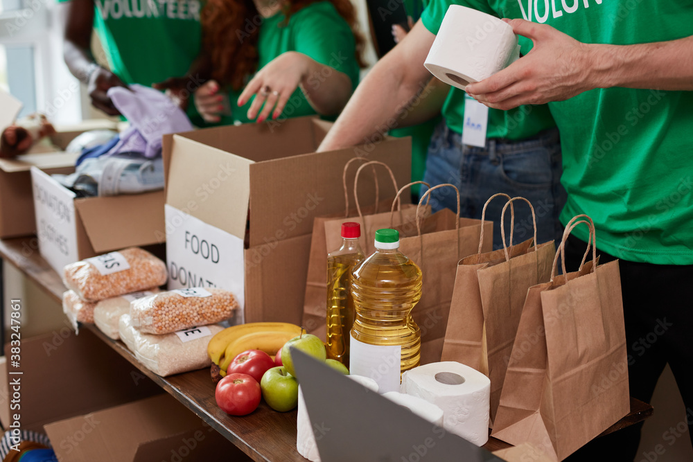 group of diverse people sort through donated food items while ...